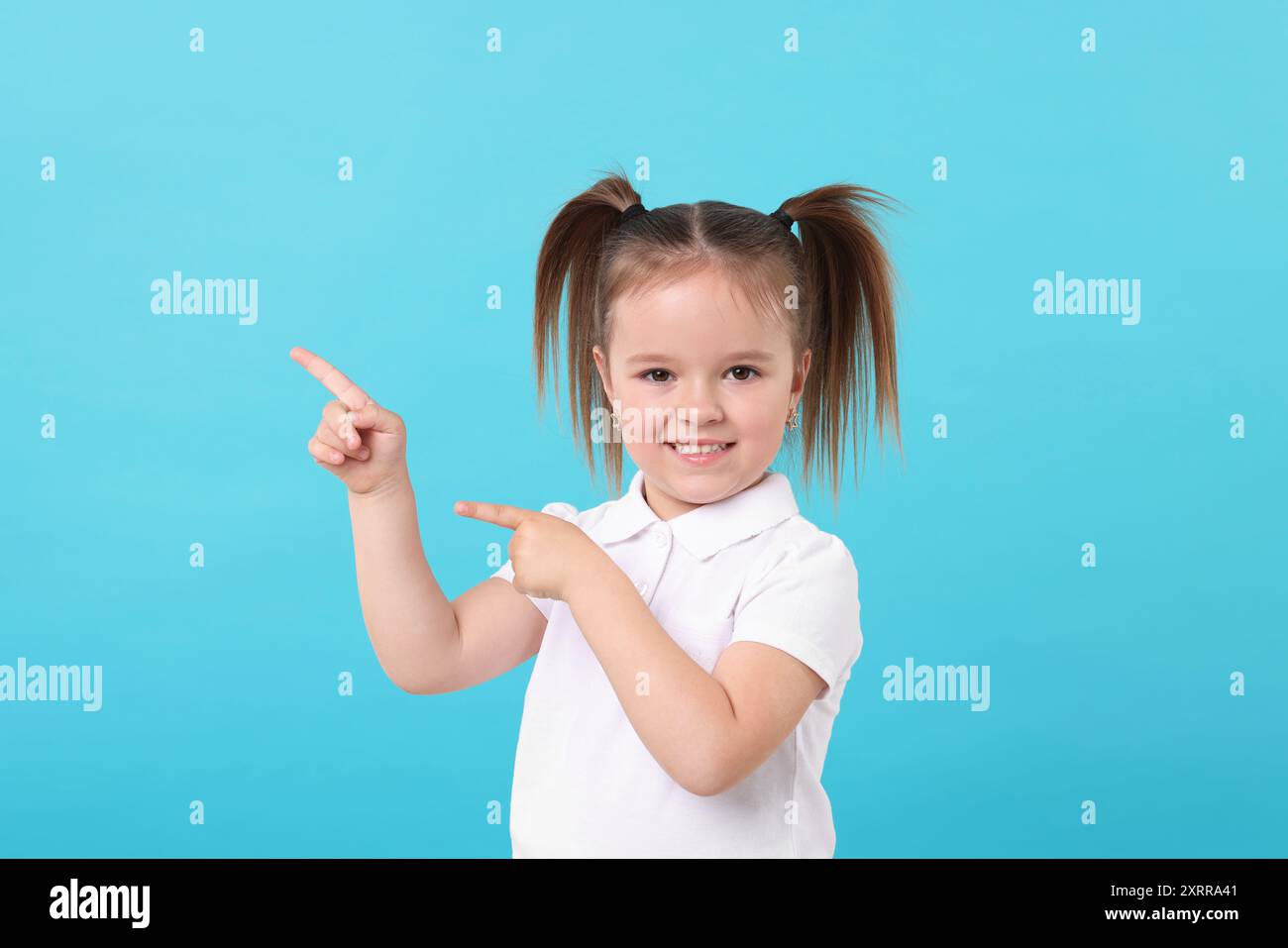 Portrait of happy little girl pointing at something on light blue ...