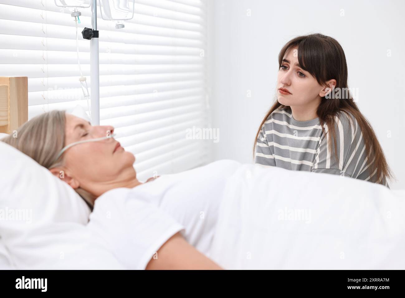 Coma patient. Sad young woman near her unconscious mother in hospital ...