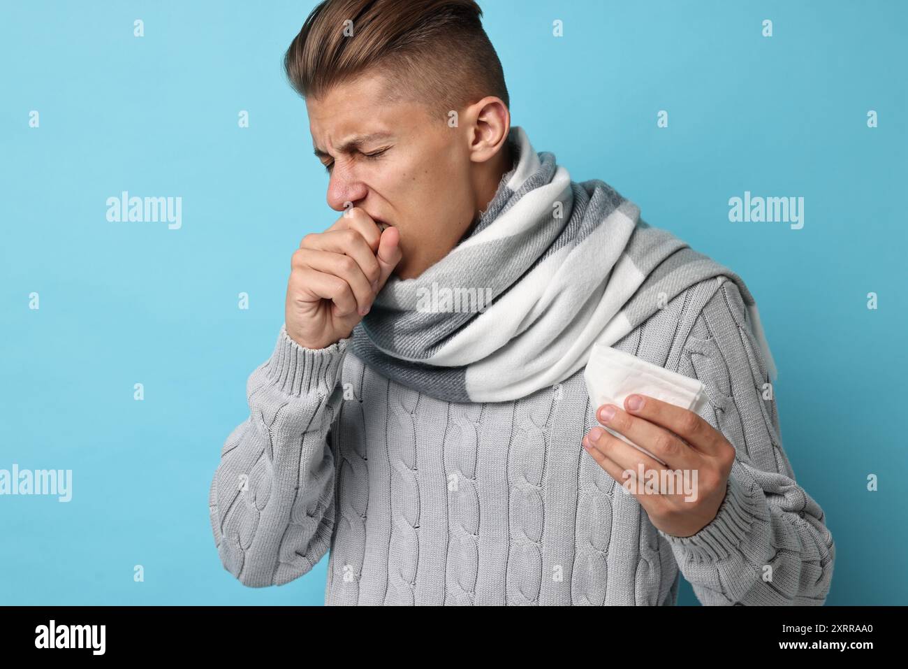 Sick man with tissue suffering from cold symptoms on light blue ...