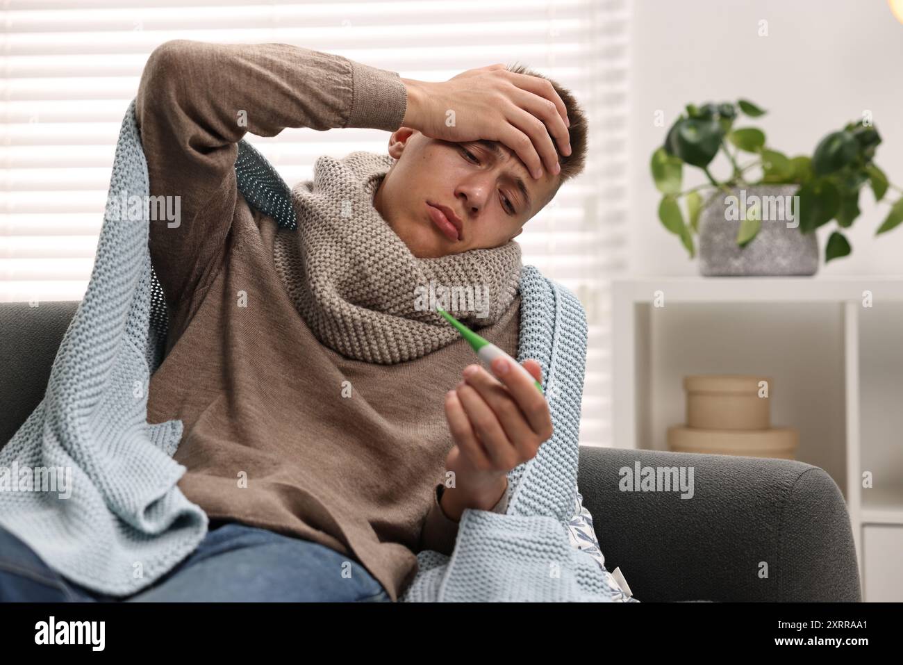 Cold symptom. Young man checking temperature with thermometer at home ...