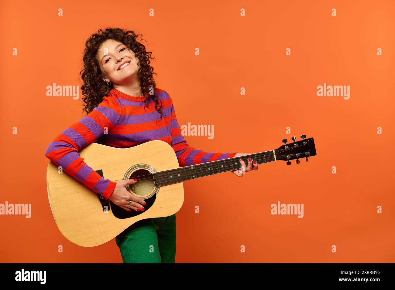 A young woman with curly hair smiles as she strums a guitar while ...