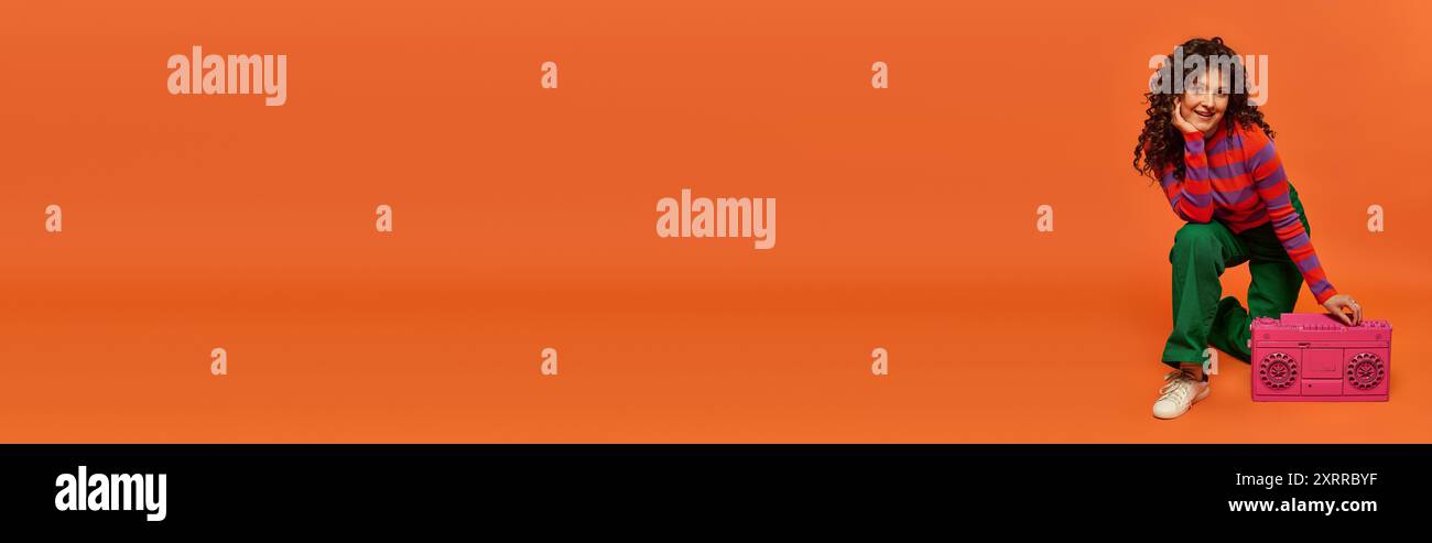 Young woman with curly hair poses against orange backdrop with pink ...