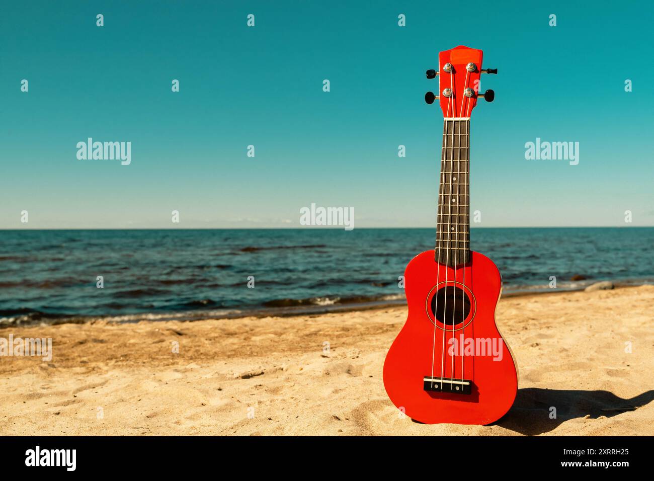 A red ukulele lies on sandy beach under sunny weather Stock Photo - Alamy