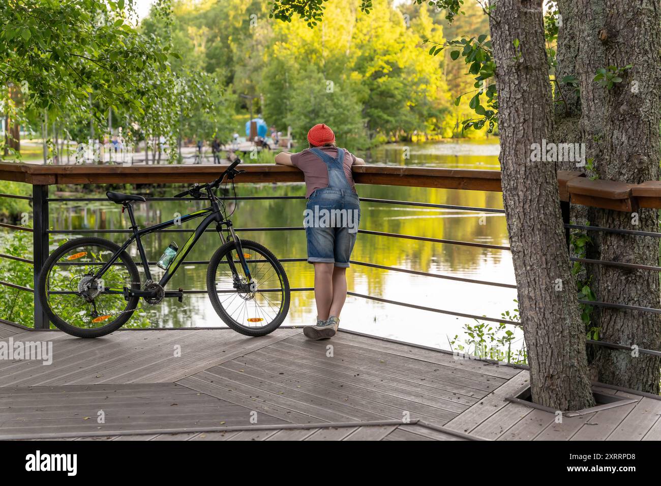 Wooman in overalls leans on railing, enjoying calm lake view , bike Stock Photo - Alamy
