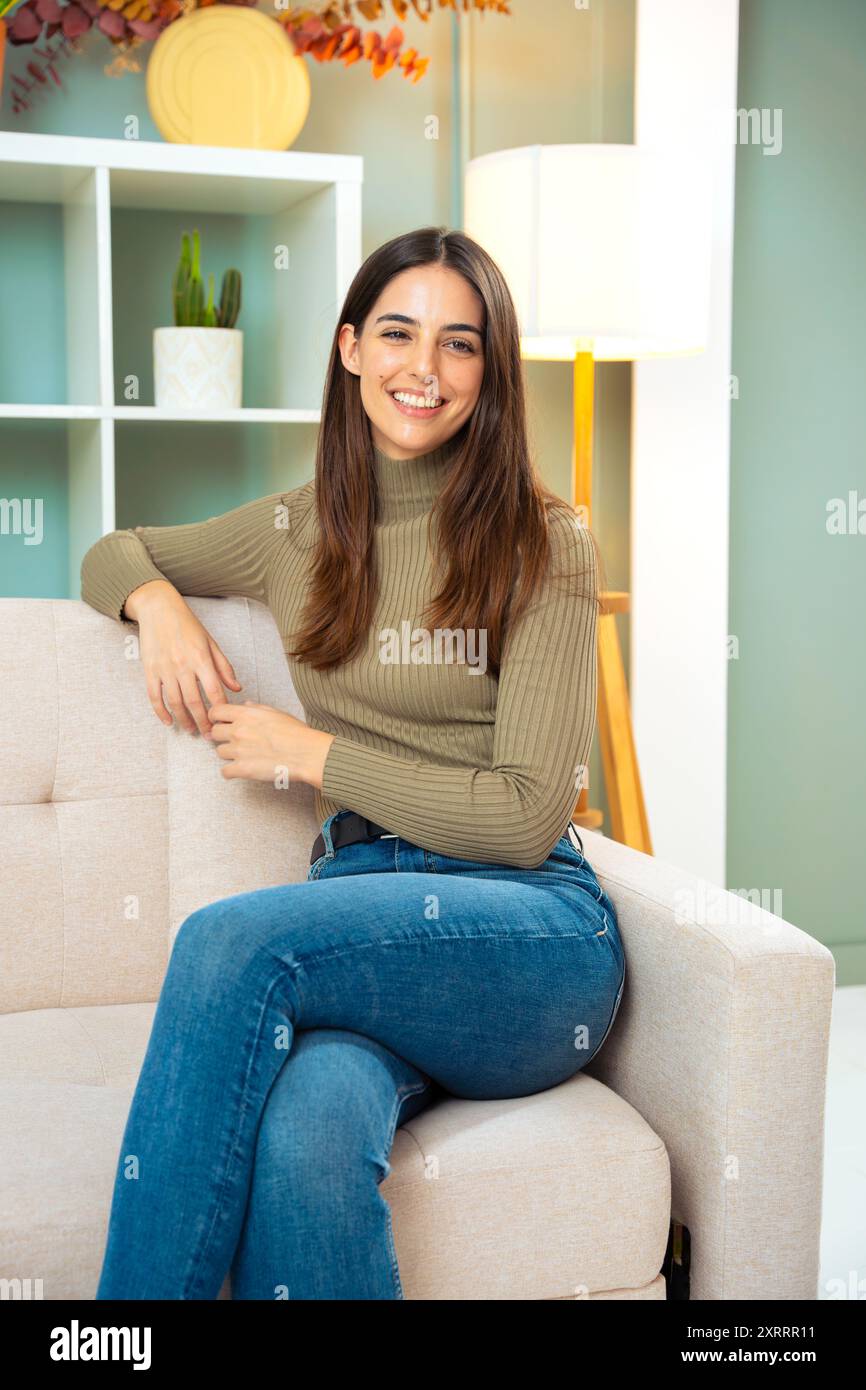 Vertical portrait young woman with a radiant smile sitting on a sofa at ...