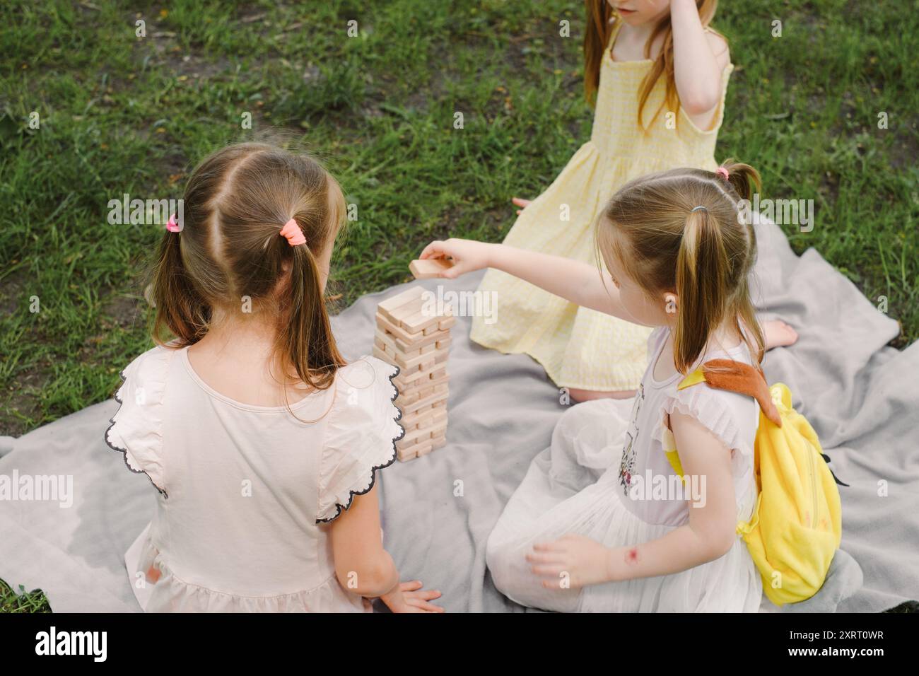 Three girls playing fun game. Children carefully stacking wooden blocks ...