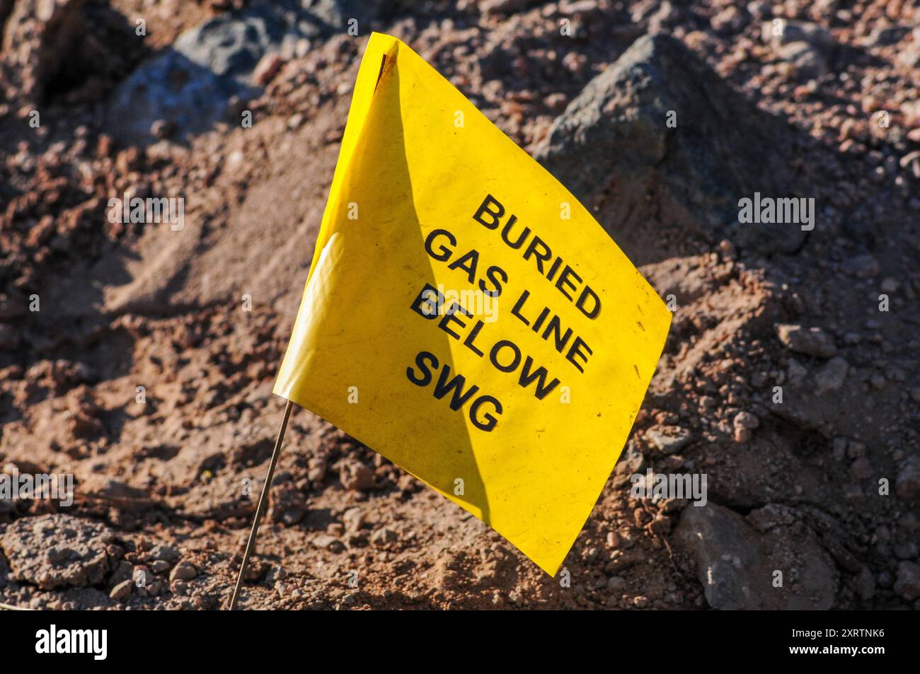 Bright yellow Buried Gas Line Below warning flag stand on a dirt lot ...