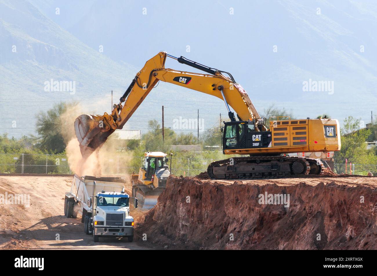 The operator of a yellow large excavator maneuvers its bucket to fill a ...