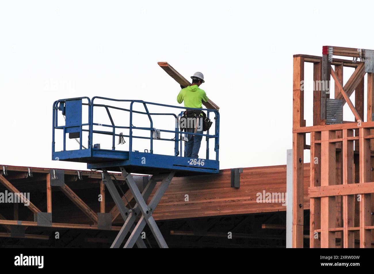 A worker using a scissor lift carrying a beam on to the rooftop of a ...
