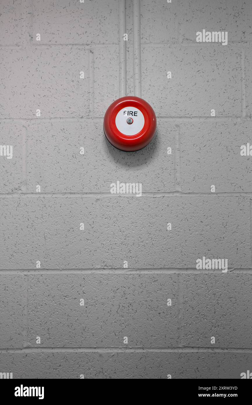 A small red fire alarm bell mounted high up on a white painted wall ...
