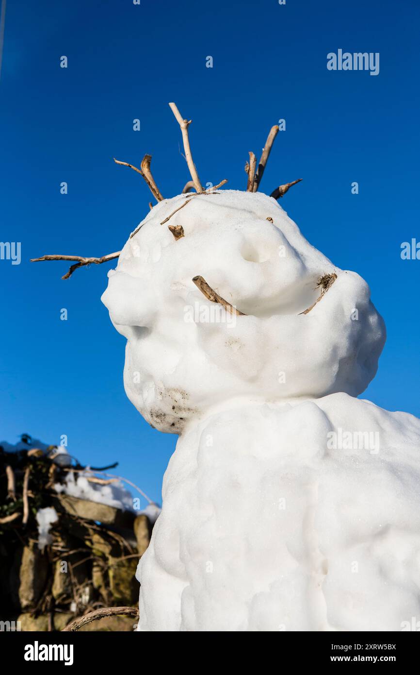 A slightly ugly, scary snowman at with blue sky built on a country lane ...