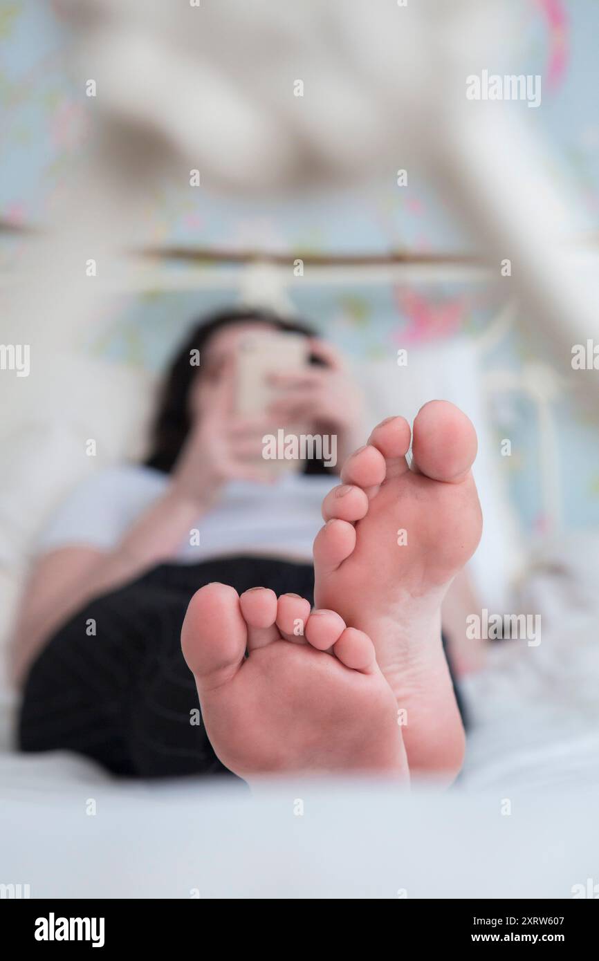 A young female looking at a her mobile phone while lying on a bed ...