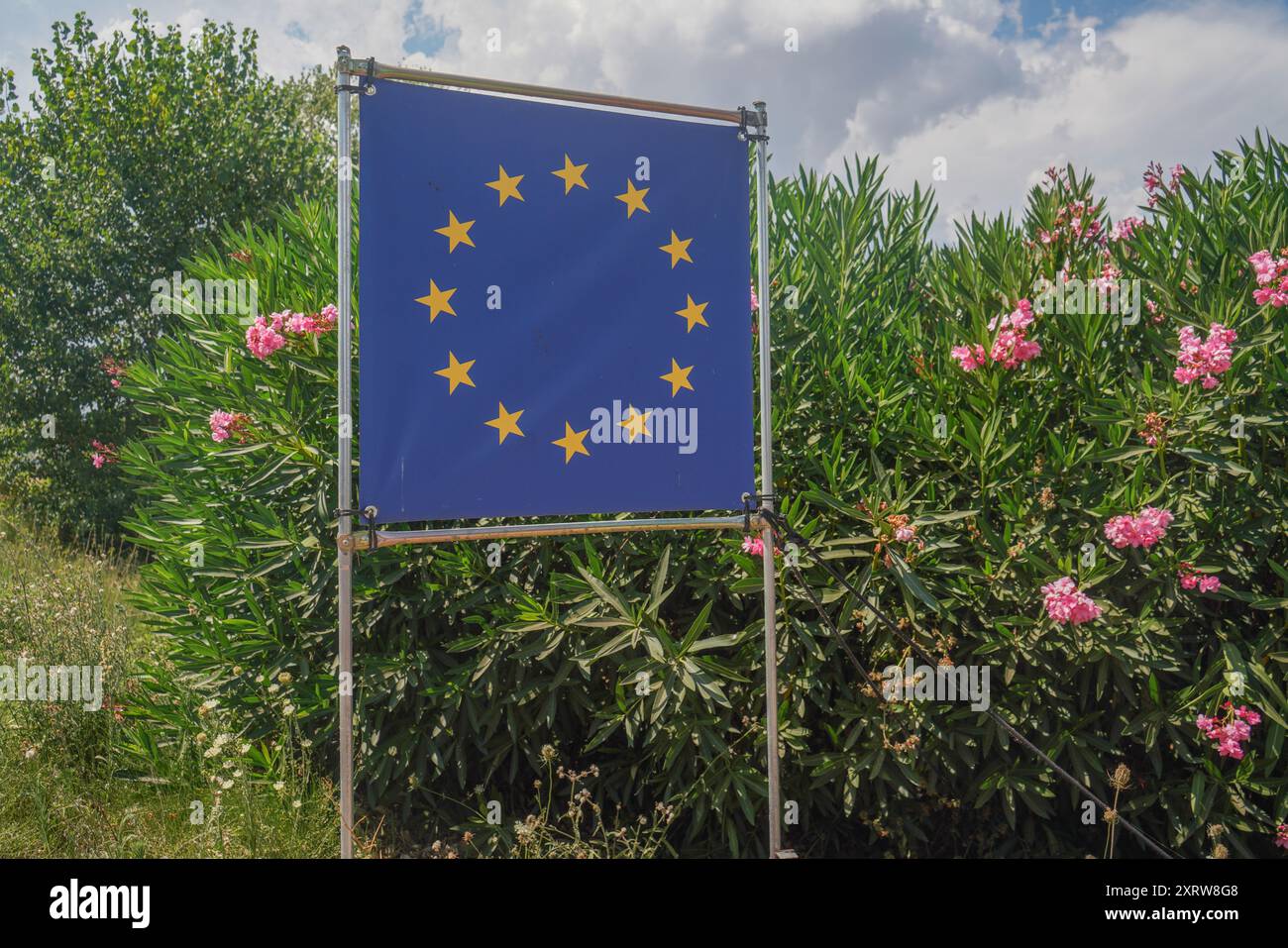 A modern road sign with the European Union Flag on blue sky with clouds ...