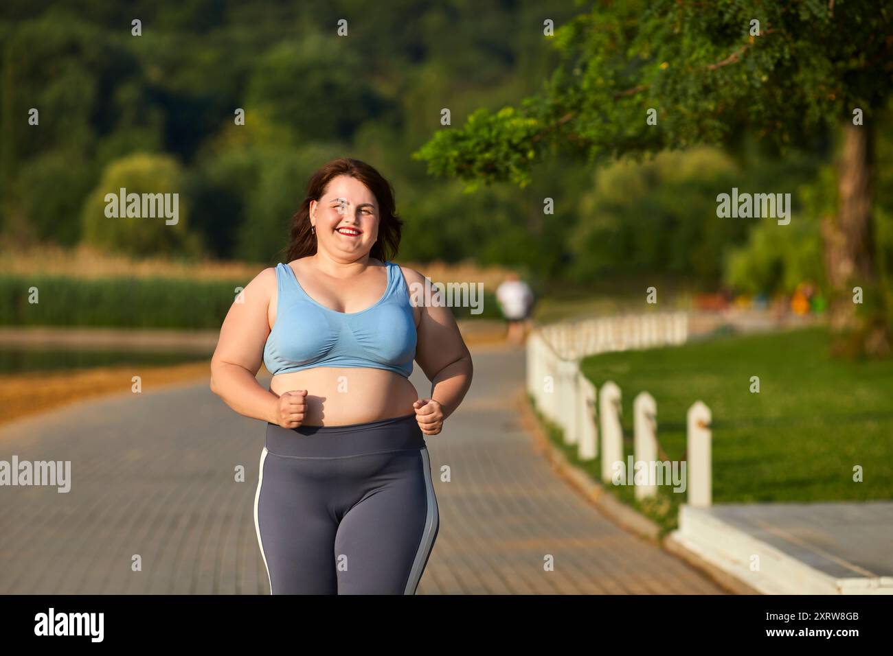 Fat happy smiling fat woman in sportswear running in the summer park ...