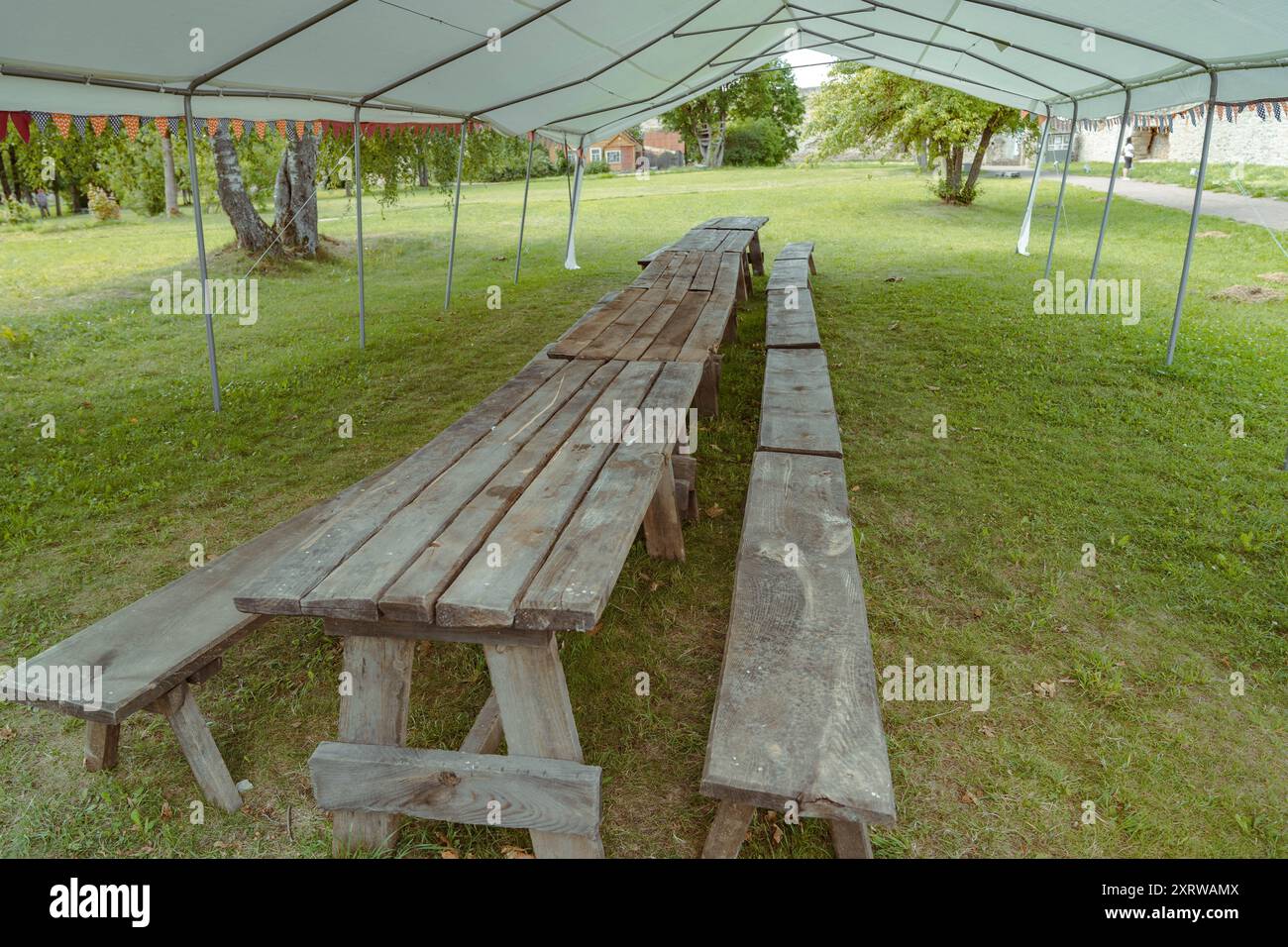 Rustic wooden tables are set under a large tent in a grassy area Stock ...