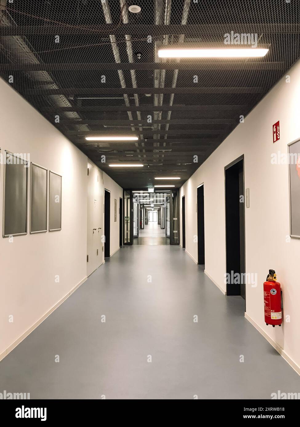 A long hallway with a red fire extinguisher on the wall. The hallway is ...
