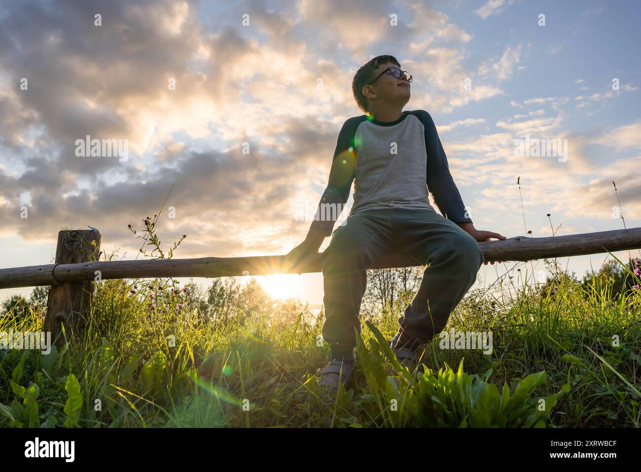 Boy sitting on a fence, watching the sunset over grassy fields Stock ...