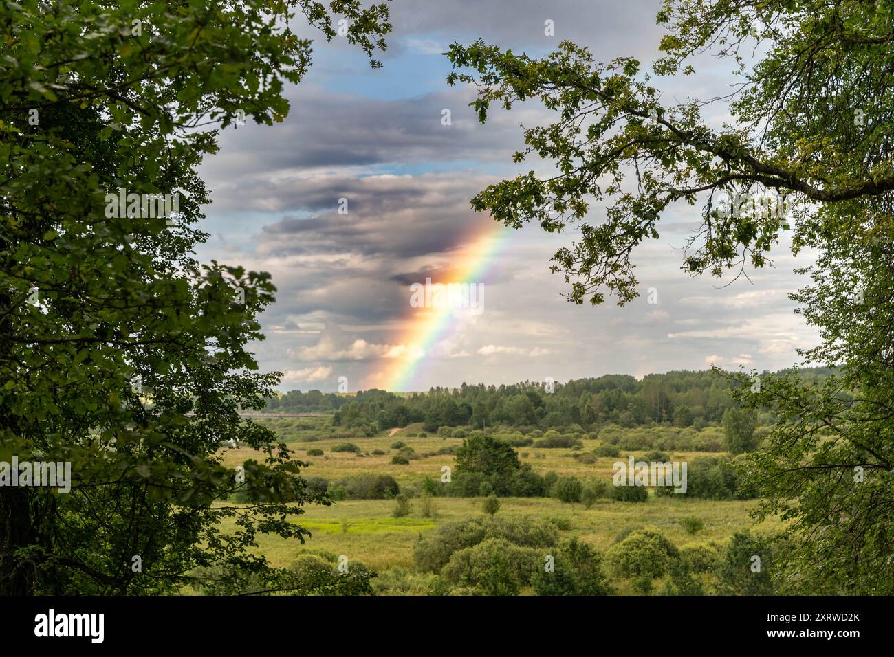 A colorful rainbow emerges over a serene countryside after rainfall ...