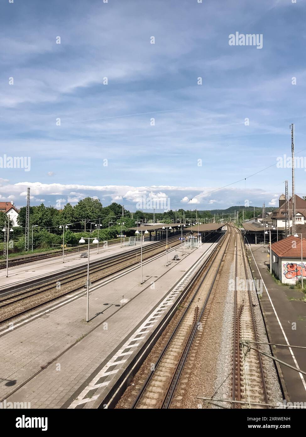 A train station with a long track of train tracks. The sky is blue and ...