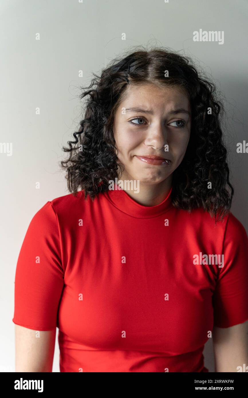 Young woman contemplates while standing by a wall with subtle lighting ...