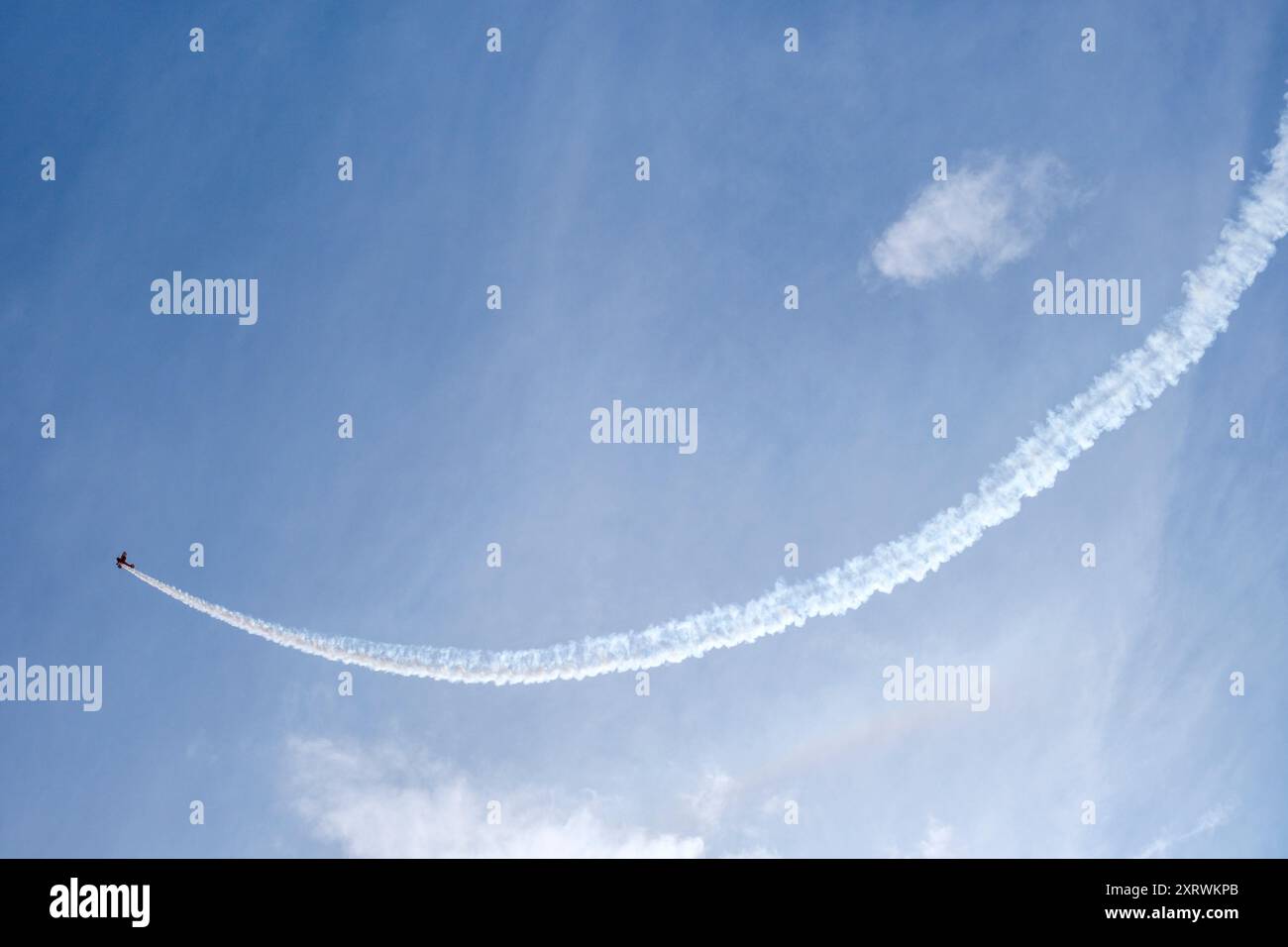 A small biplane permorms aerobatic loops trtailing vapor in a blue sky ...