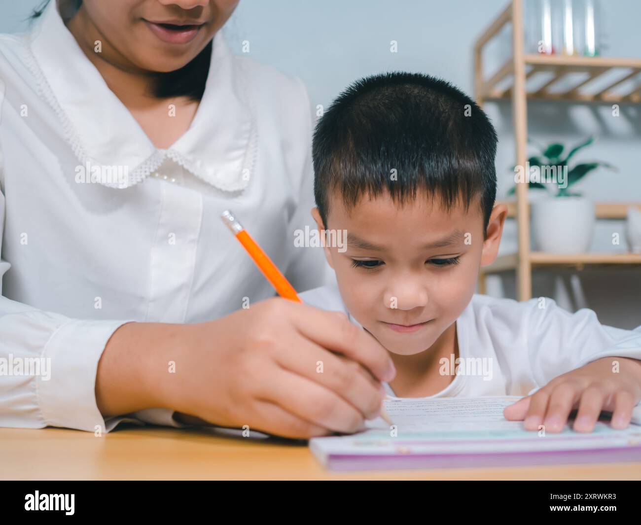 Teacher or mother helping boy writing lesson and learning to write, Female tutor helping little ...