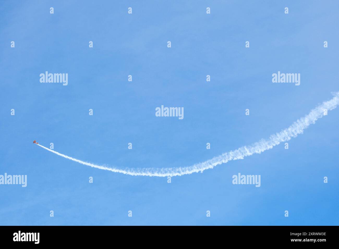 A small biplane permorms aerobatic loops trtailing vapor in a blue sky ...