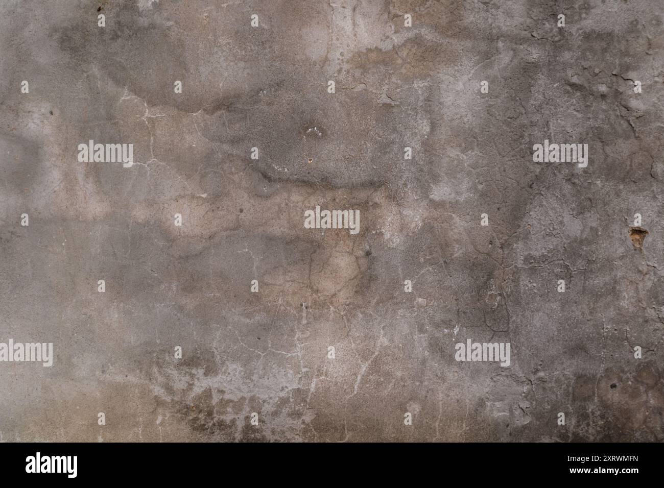 A grey wall with cracks and holes. The wall is rough and uneven, giving ...