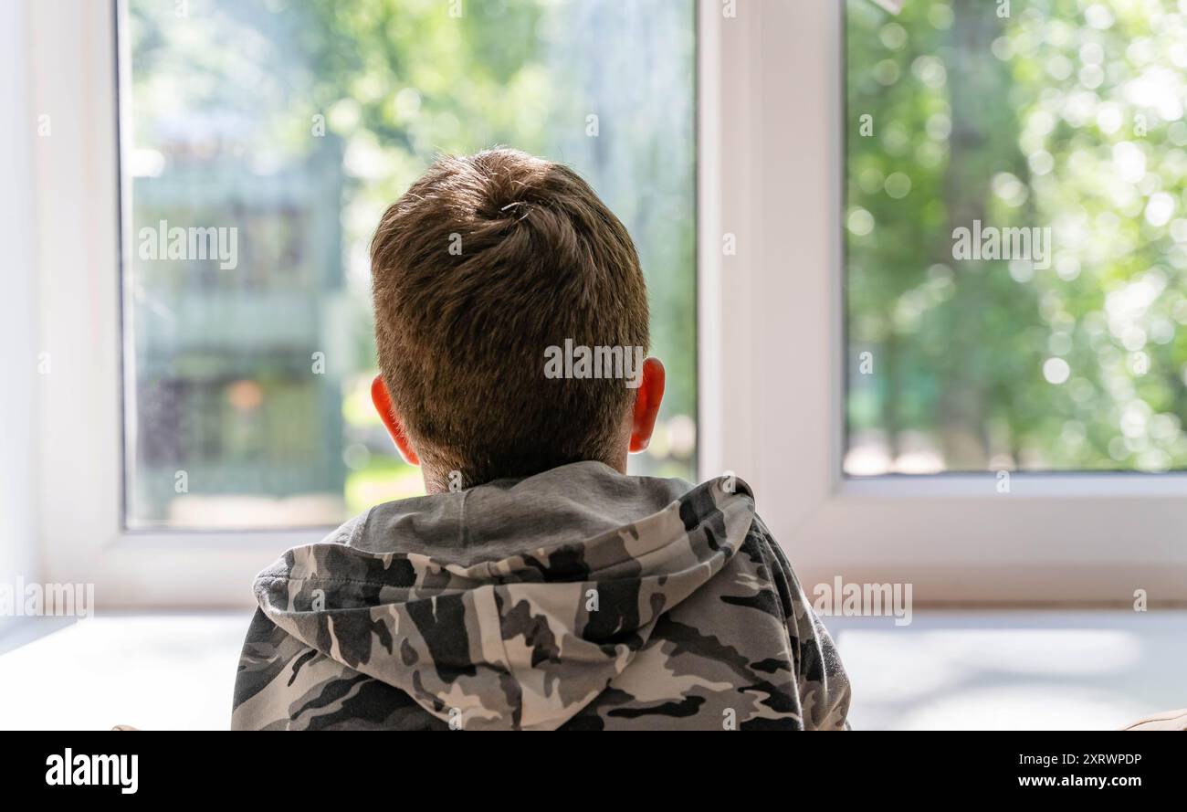 Boy observes nature outside through a bright, clear window. sad child ...