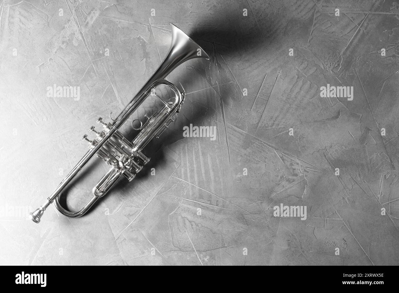 Shiny trumpet on grey textured table, top view. Space for text. Wind ...