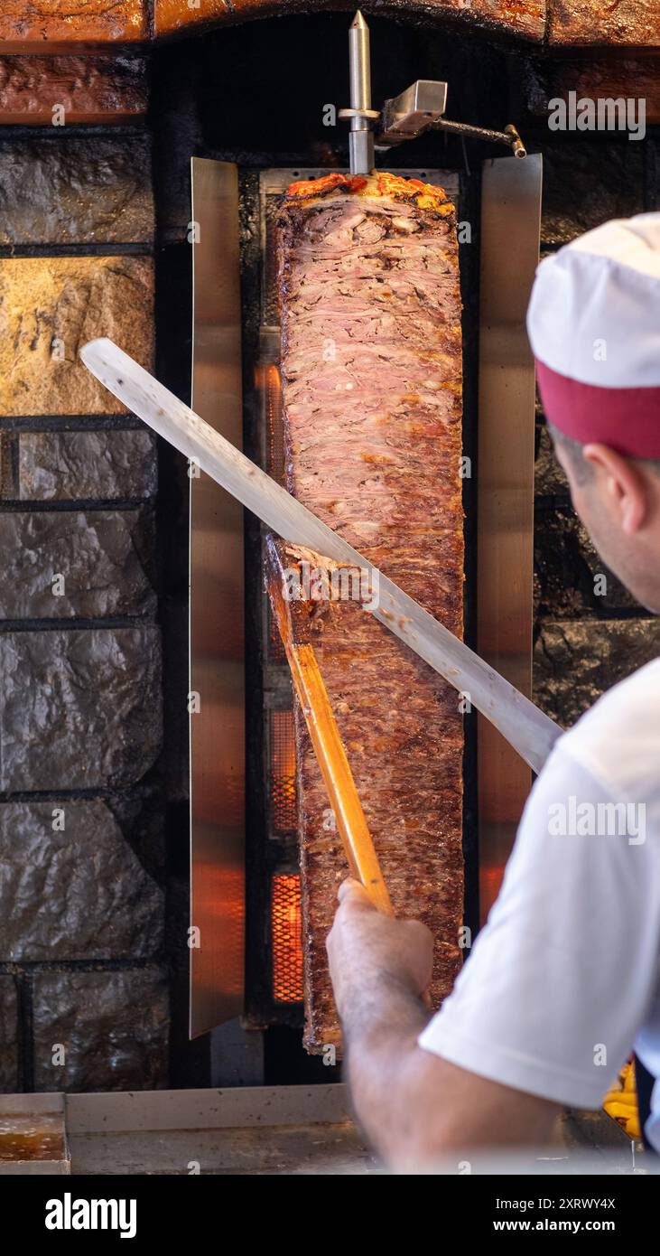 Chef skillfully cutting shawarma meat from a rotating skewer. Freshly ...