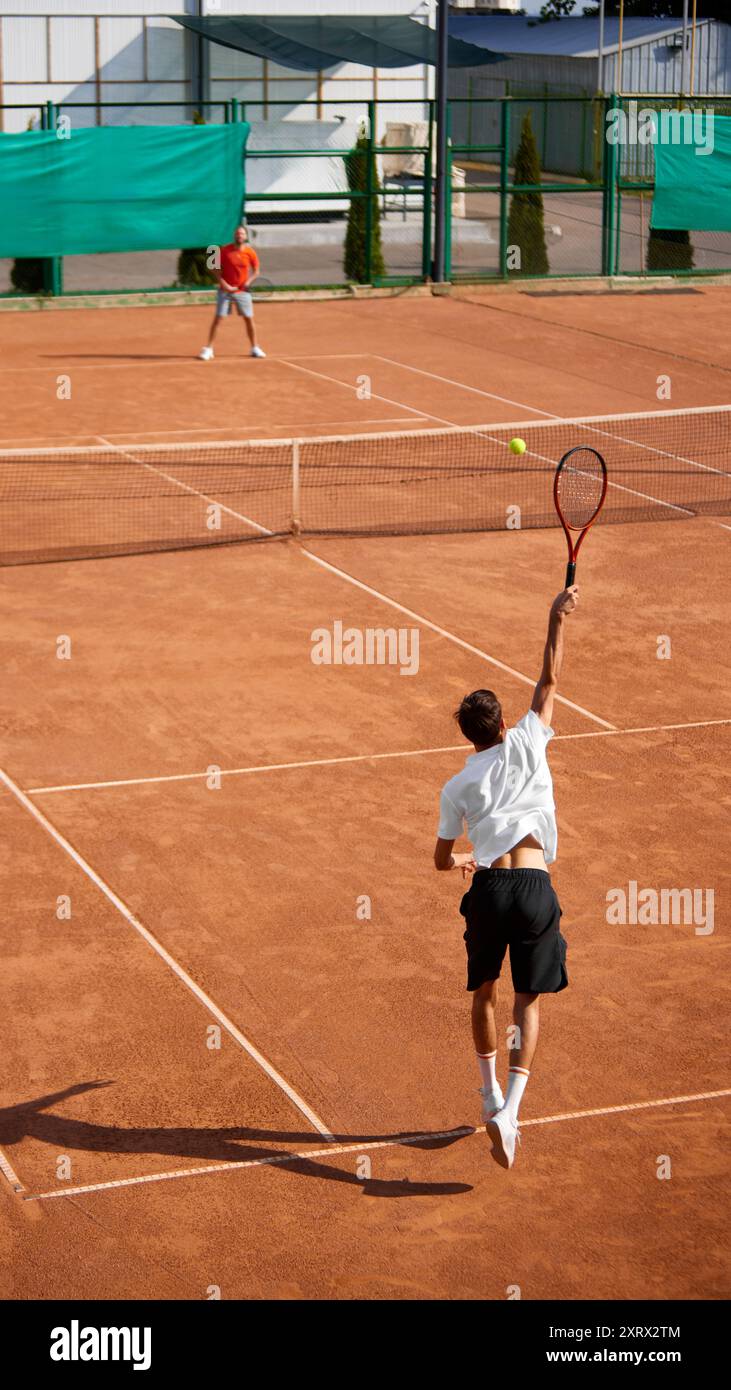 Vertical image of two men, tennis players in motion on clay court ...