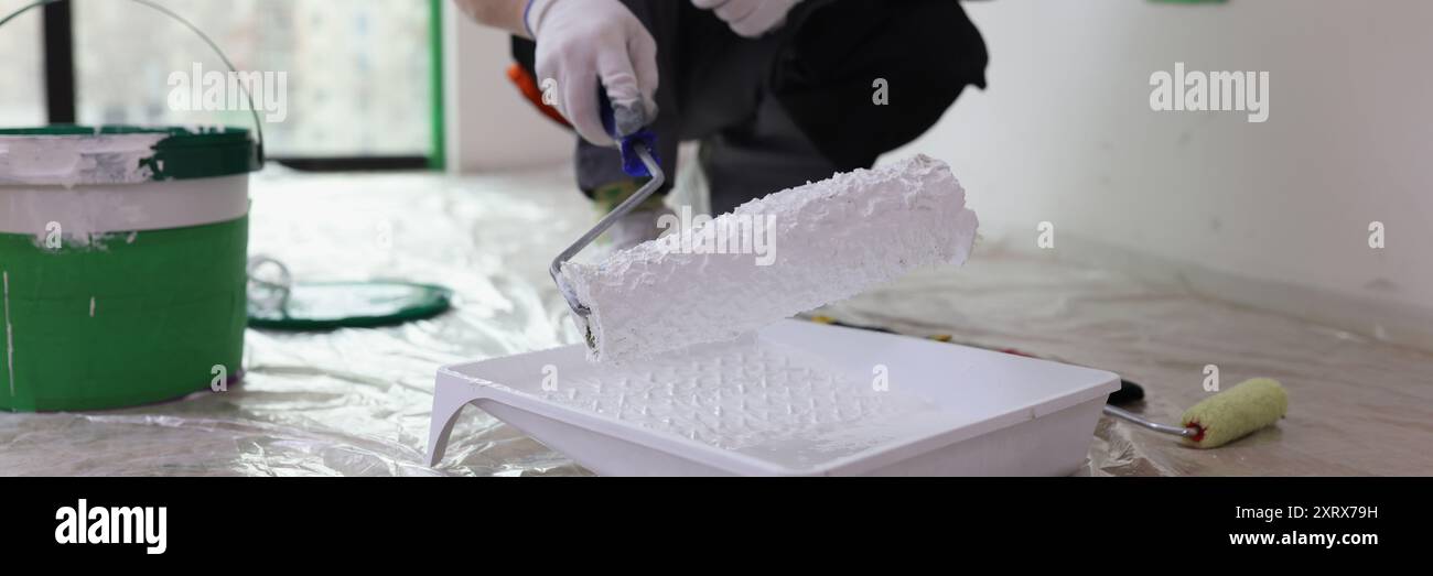 Male builder in uniform holding roller with white paint Stock Photo - Alamy