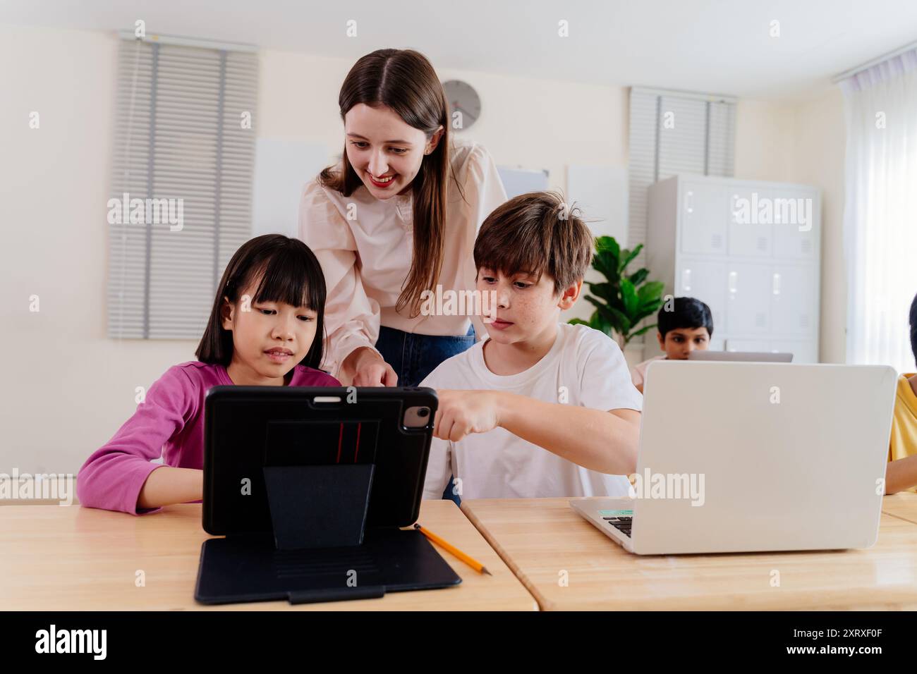 Young teacher guides diverse students with digital devices in modern ...