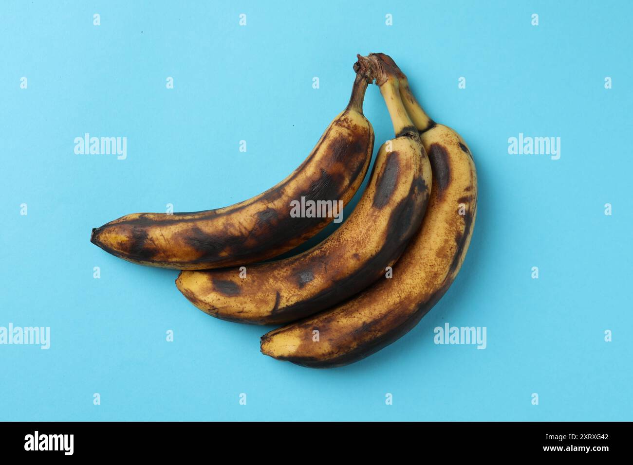 Bunch of ripe bananas with dark spots on light blue background, top ...