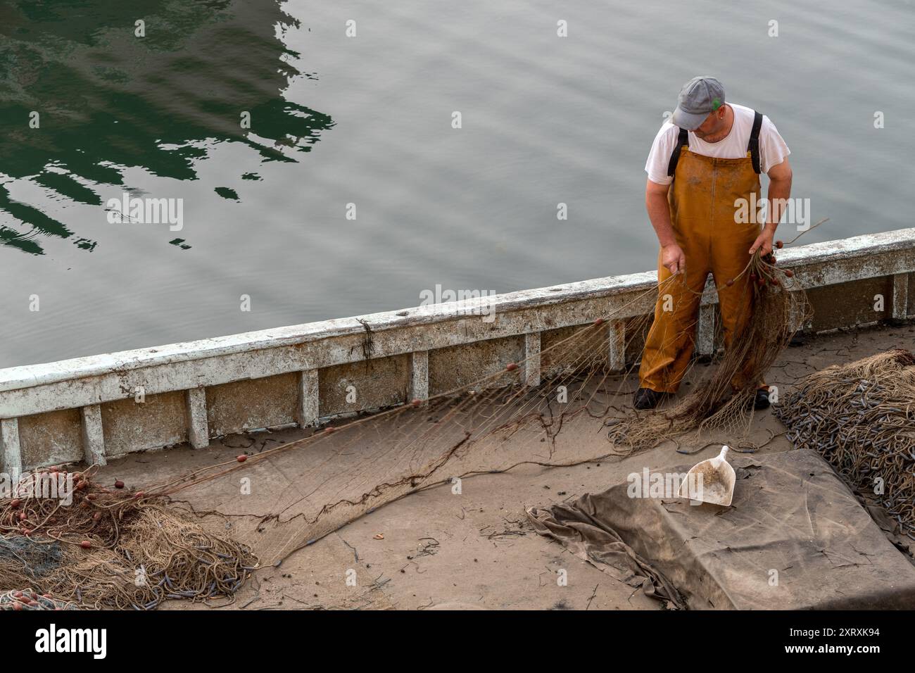 Fisherman arranges Fishing Nets on the edge of his fishing Boat docked ...