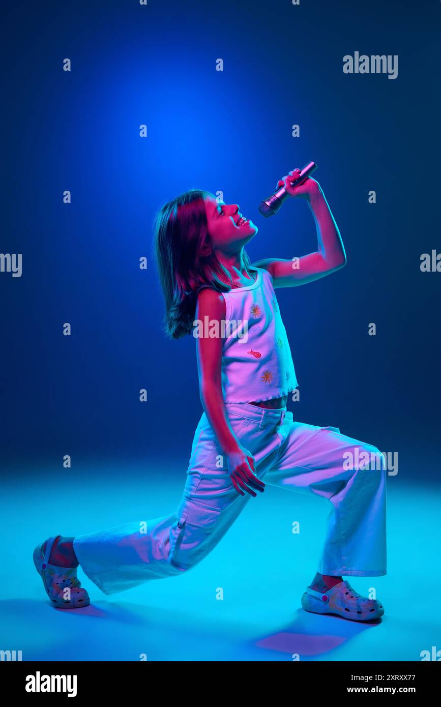 Young positive, emotional girl in white clothes singing in microphone ...