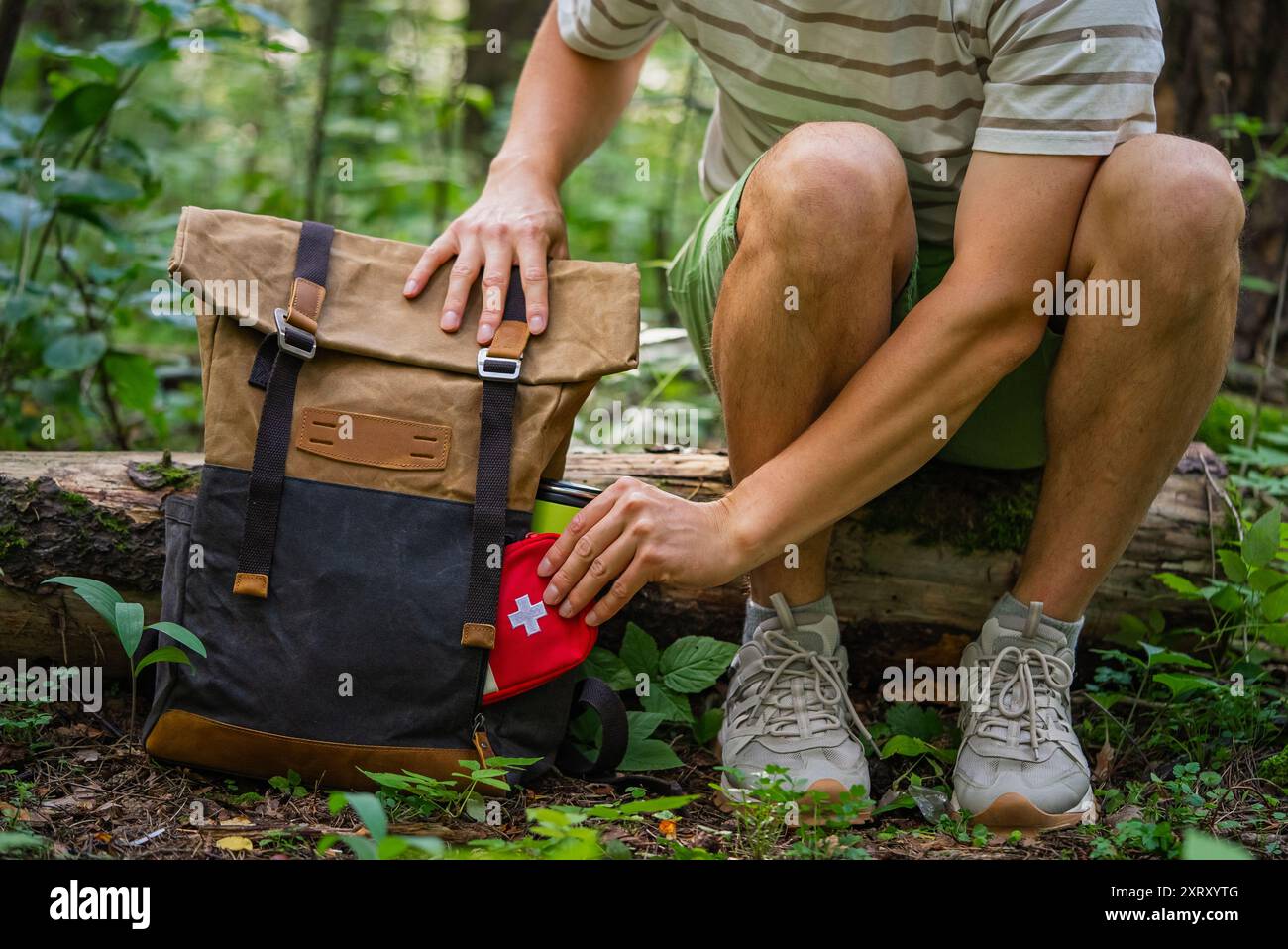 Hiker man crouching in a forest, packing a first aid kit into a ...