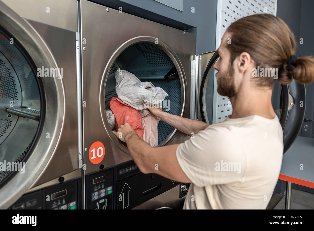 Busy man doing household chores loading washing machine at public ...