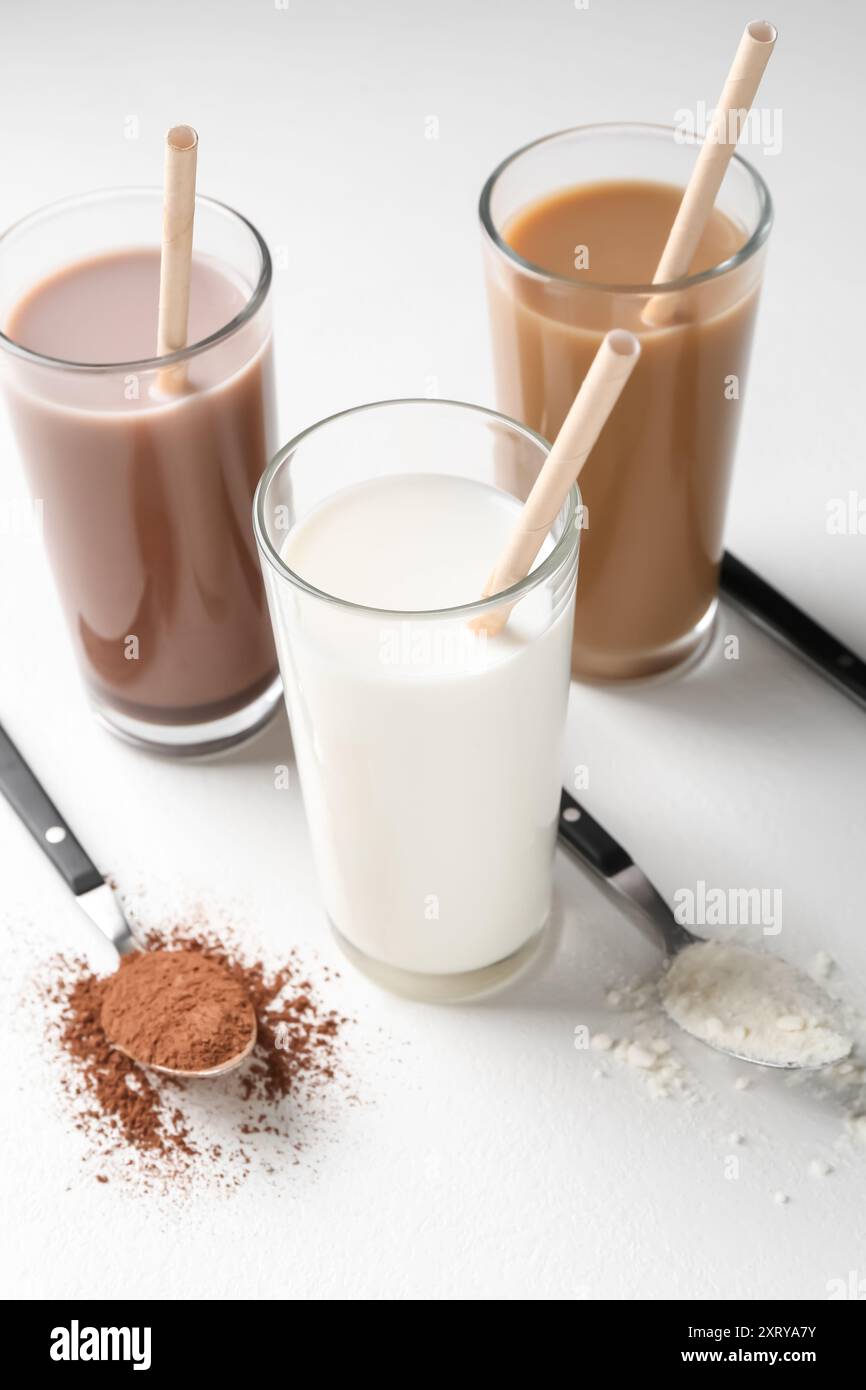 Delicious protein shakes in glasses and spoons with powder on white ...