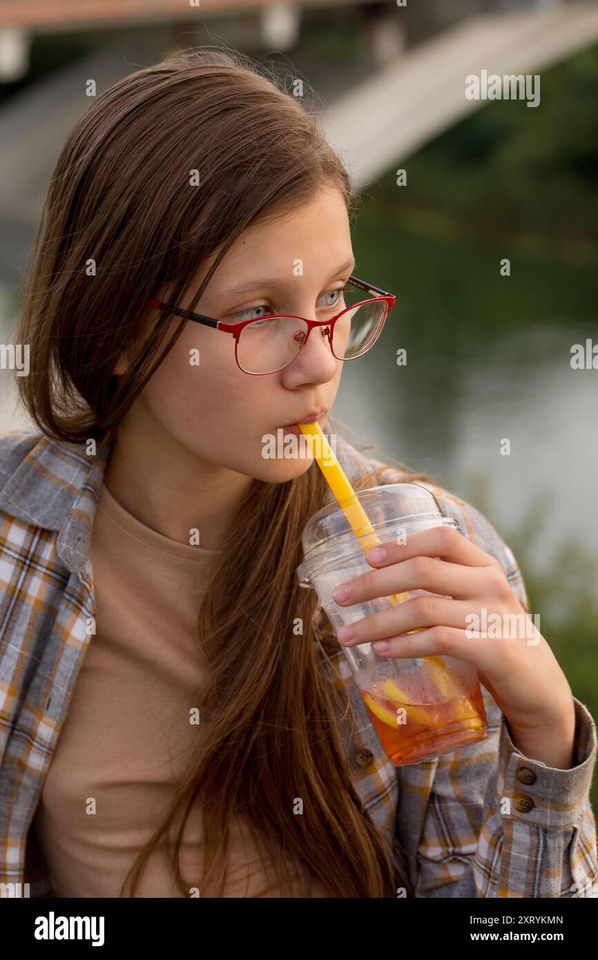 A teenage girl in glasses drinks bubble tea on a walk on the city ...