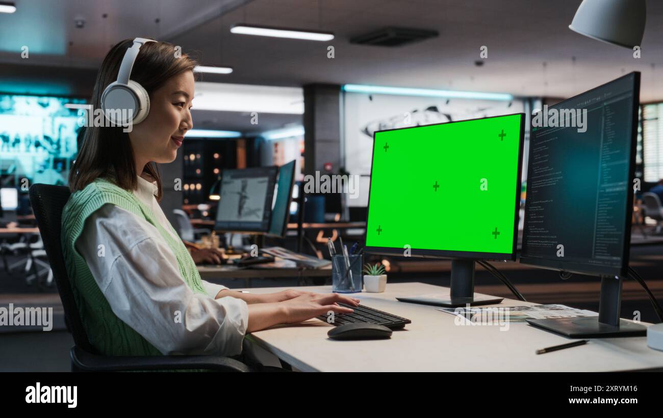Female Asian Game Programmer Coding On Desktop Computer With Green Screen Chromakey On Display