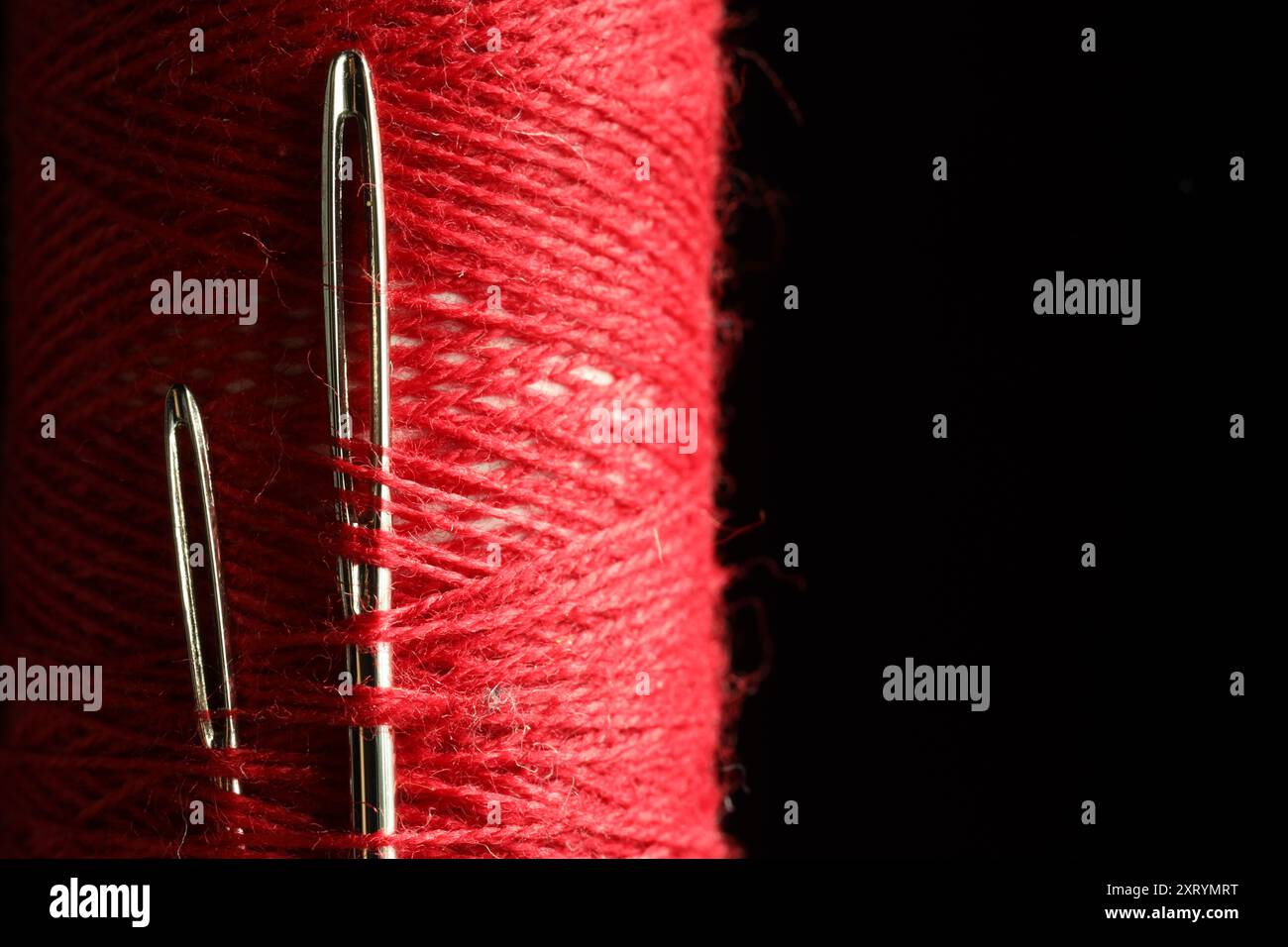 Spool of red sewing thread with needles on black background, closeup ...