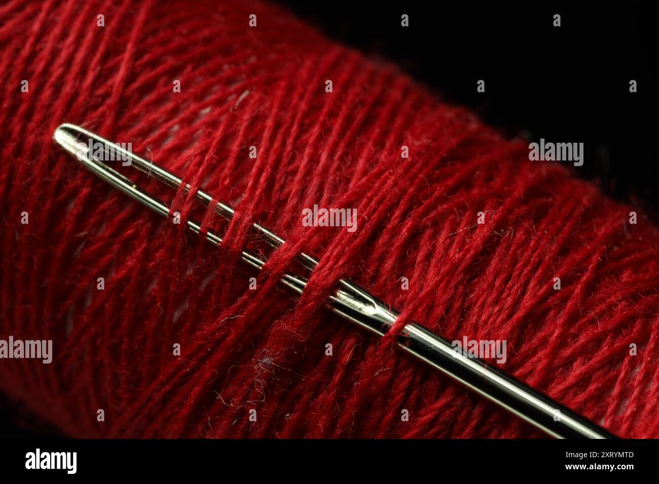 Spool of red sewing thread with needle on black background, closeup ...