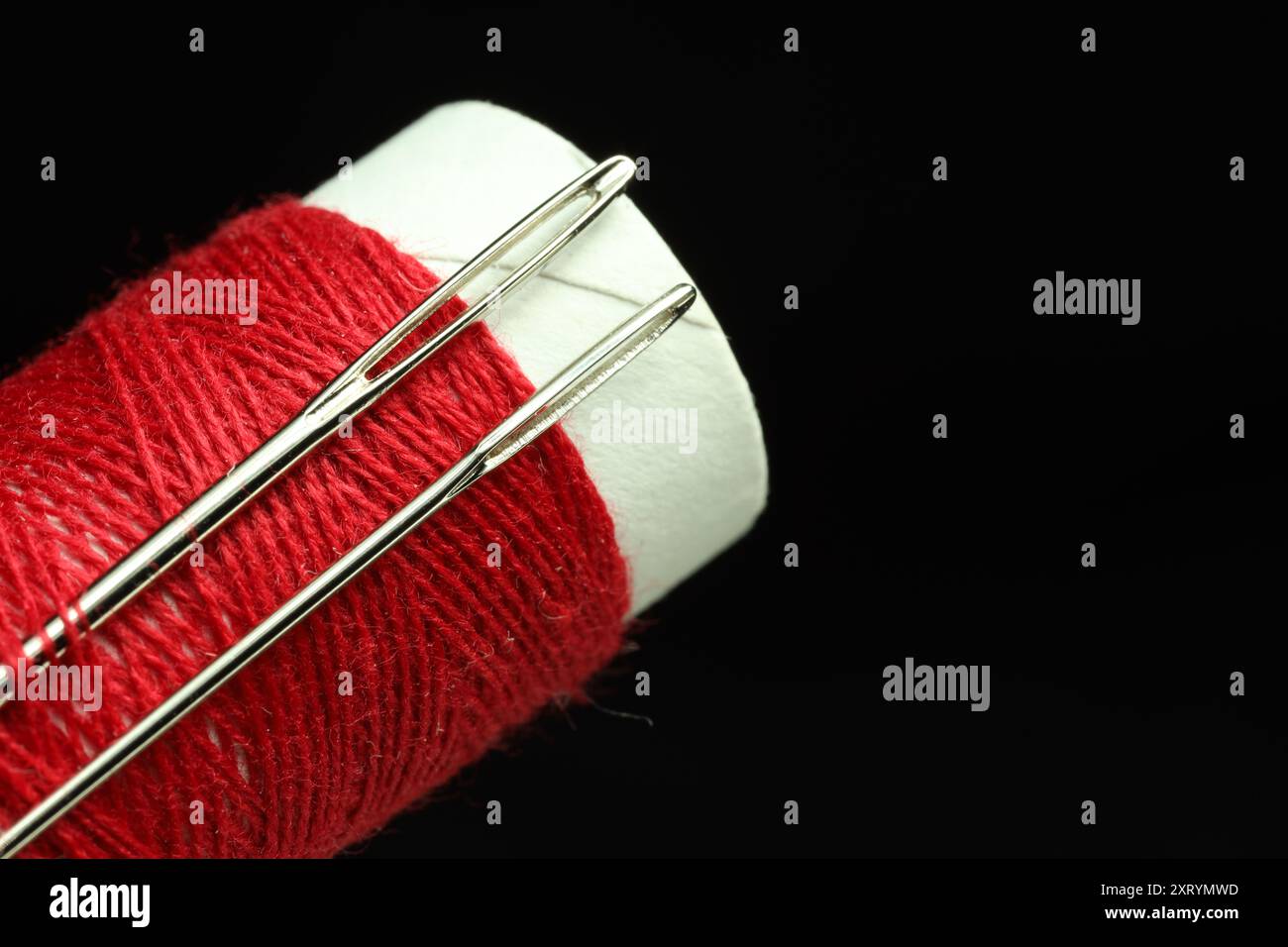Spool of red sewing thread with needles on black background, closeup ...