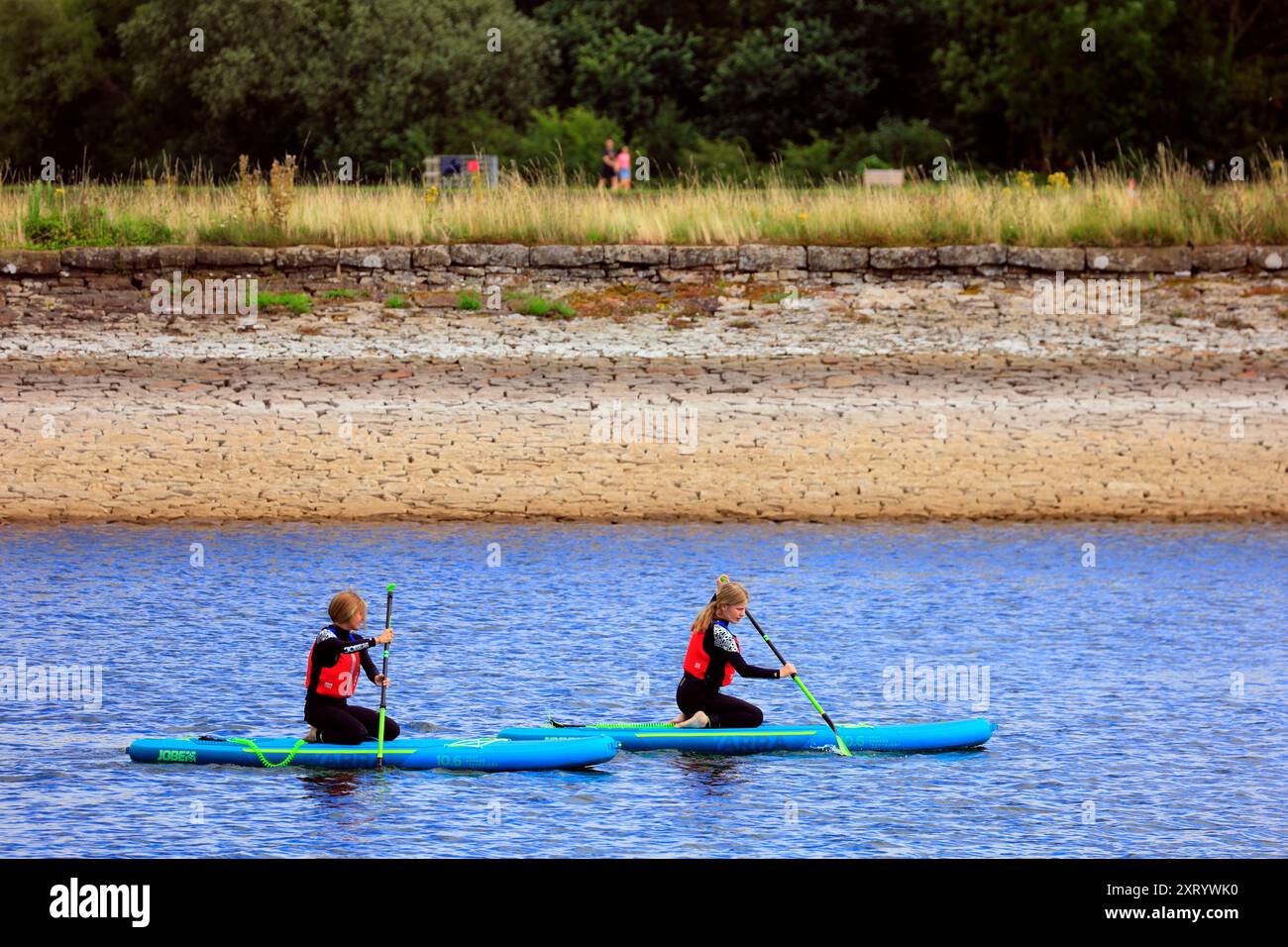 Two girls kneeling on paddle boards and wearing safety life vests ...