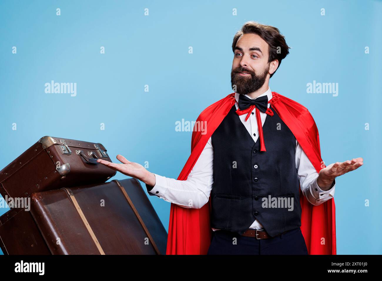 Hotel employee wears red cape to help travellers with luggage, pretending to be comic cartoon ...