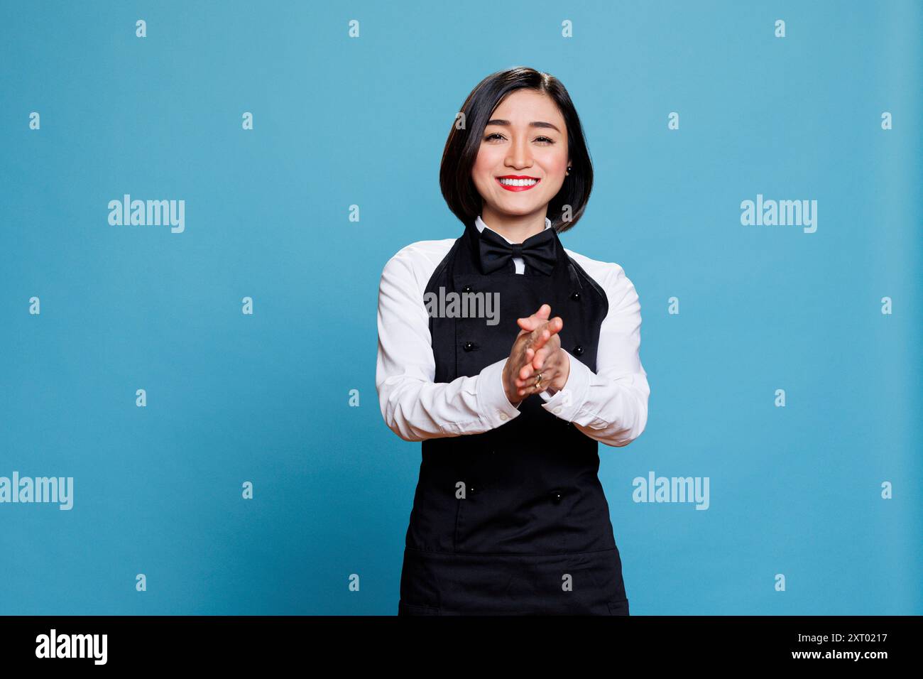 Smiling asian waitress wearing uniform applauding with to show support ...