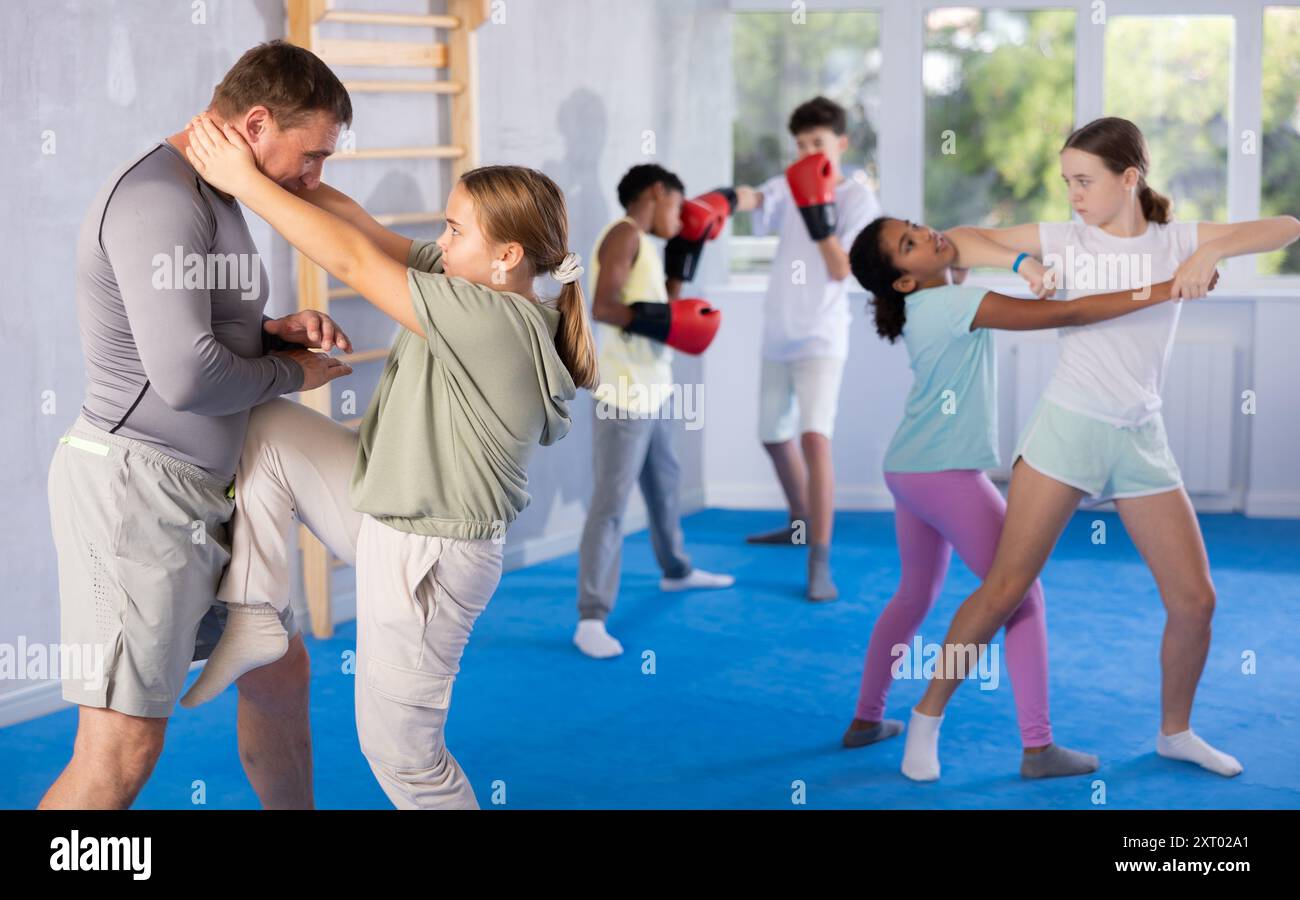 Tween girl performing knee strike in midsection to instructor in self ...