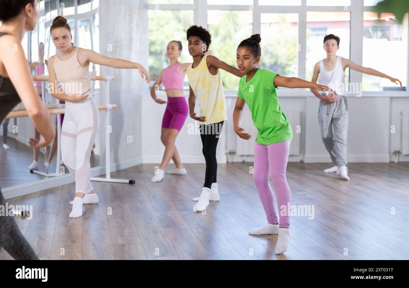 African American preteen girl practicing ballet movements during group ...